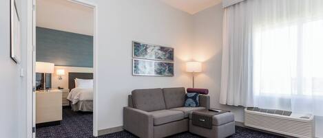 Quarto de hotel com sofá, mesa pequena, luminária, cama e janela com cortinas.