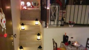 Uma escadaria com lanternas fixadas na parede, uma sala de jantar com uma mesa posta para dois e uma parede decorativa com motivos de coração.