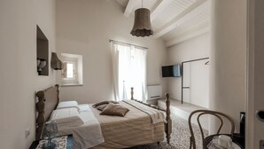 Quarto com cama, mesa de cabeceira, cadeira e televisão na parede.