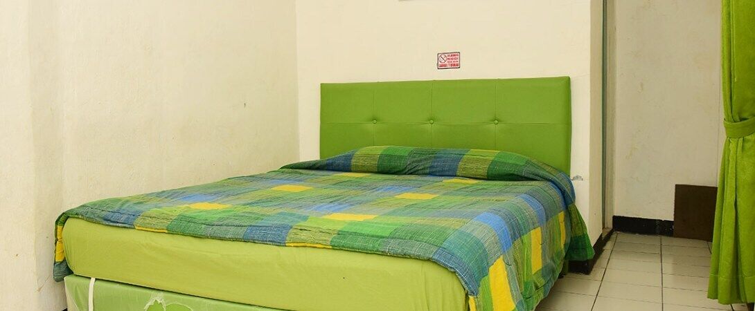Uma cama de solteiro com cabeceira verde e colcha colorida.