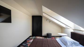 Quarto com cama, uma mesa redonda pequena e televisão na parede.