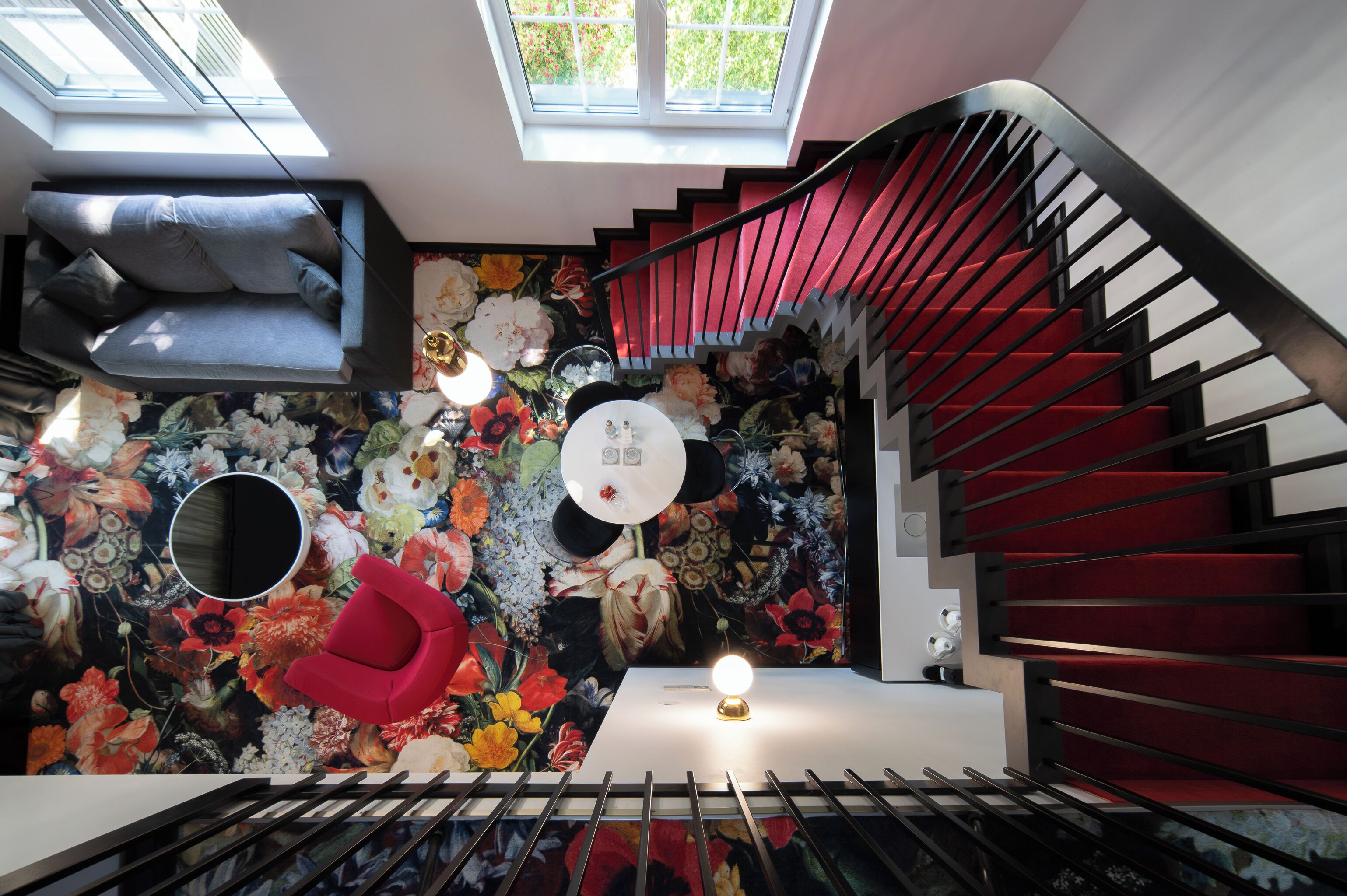 Um interior moderno com uma escada vermelha, um claraboia e um mural floral na parede.
