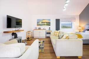 Uma sala de estar moderna com televisão de tela plana, um conjunto de sofás, um espaço de refeições e uma cozinha.