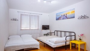 Quarto com duas camas, televisão, quadro e uma pequena mesa com uma planta.