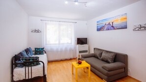 Uma sala de estar com sofá, cama, mesa de centro de madeira e televisão.