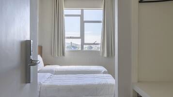 Quarto de hotel com duas camas, uma janela com cortinas, um radiador e um cabideiro.