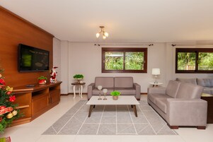 Uma sala de estar com televisão, dois sofás, uma mesa de centro e um pinheiro de Natal.