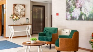 Um hall moderno com uma mesa de recepção de madeira, uma poltrona verde, uma poltrona marrom e uma pequena mesa com uma planta.