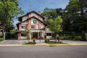 Hotel com fachada de tijolos, placa verde e entrada pavimentada.