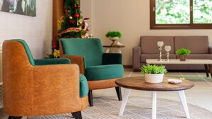 Uma sala de estar com uma poltrona verde, uma poltrona marrom, uma mesa de centro de madeira com uma planta, um pinheiro de Natal e um sofá.