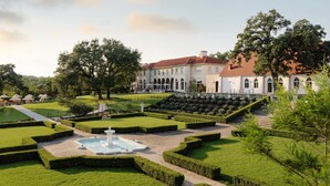 Um edifício grande e histórico com um jardim formal, incluindo uma fonte e sebes bem aparadas.