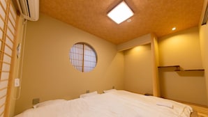 Quarto de hotel com uma cama grande, uma janela redonda, uma luminária no teto e piso de madeira.