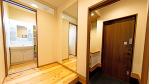 Um corredor com piso de madeira, um espelho refletindo um banheiro e uma porta de madeira.