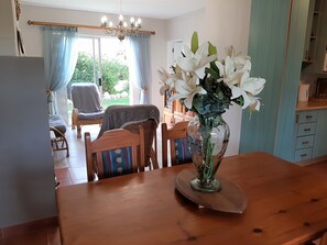 Uma sala de jantar com mesa de madeira, cadeiras e um vaso de flores brancas.