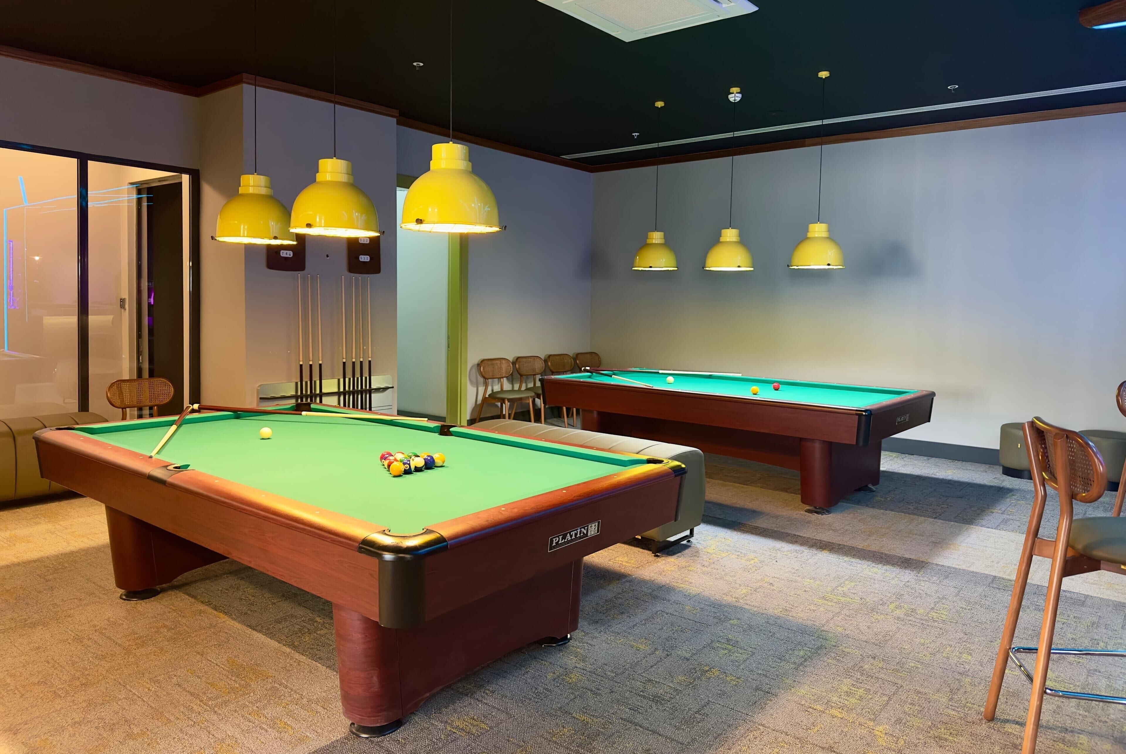 Uma mesa de bilhar com feltro verde, uma bola de bilhar vermelha e uma luminária pendente amarela.