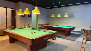 Uma mesa de bilhar com feltro verde, uma bola de bilhar vermelha e uma luminária pendente amarela.
