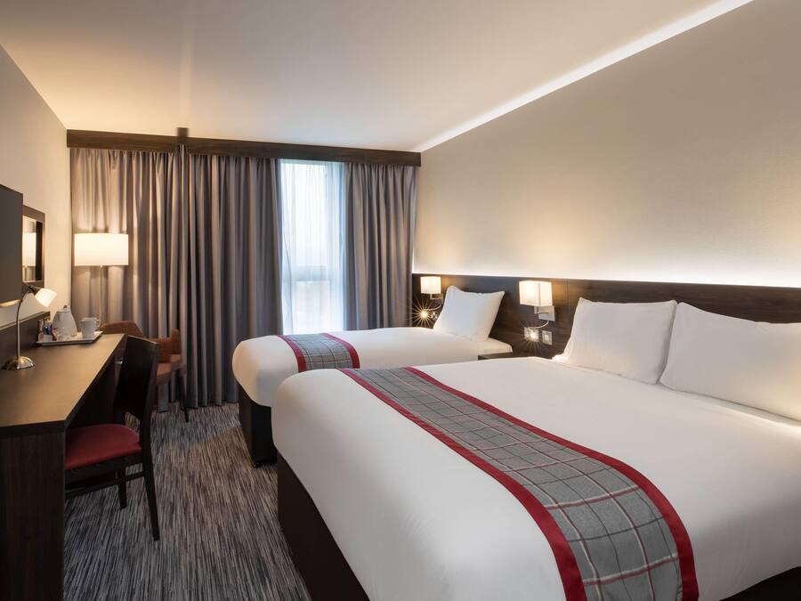 Quarto de hotel com duas camas, uma escrivaninha, uma cadeira, uma televisão e uma janela com cortinas.