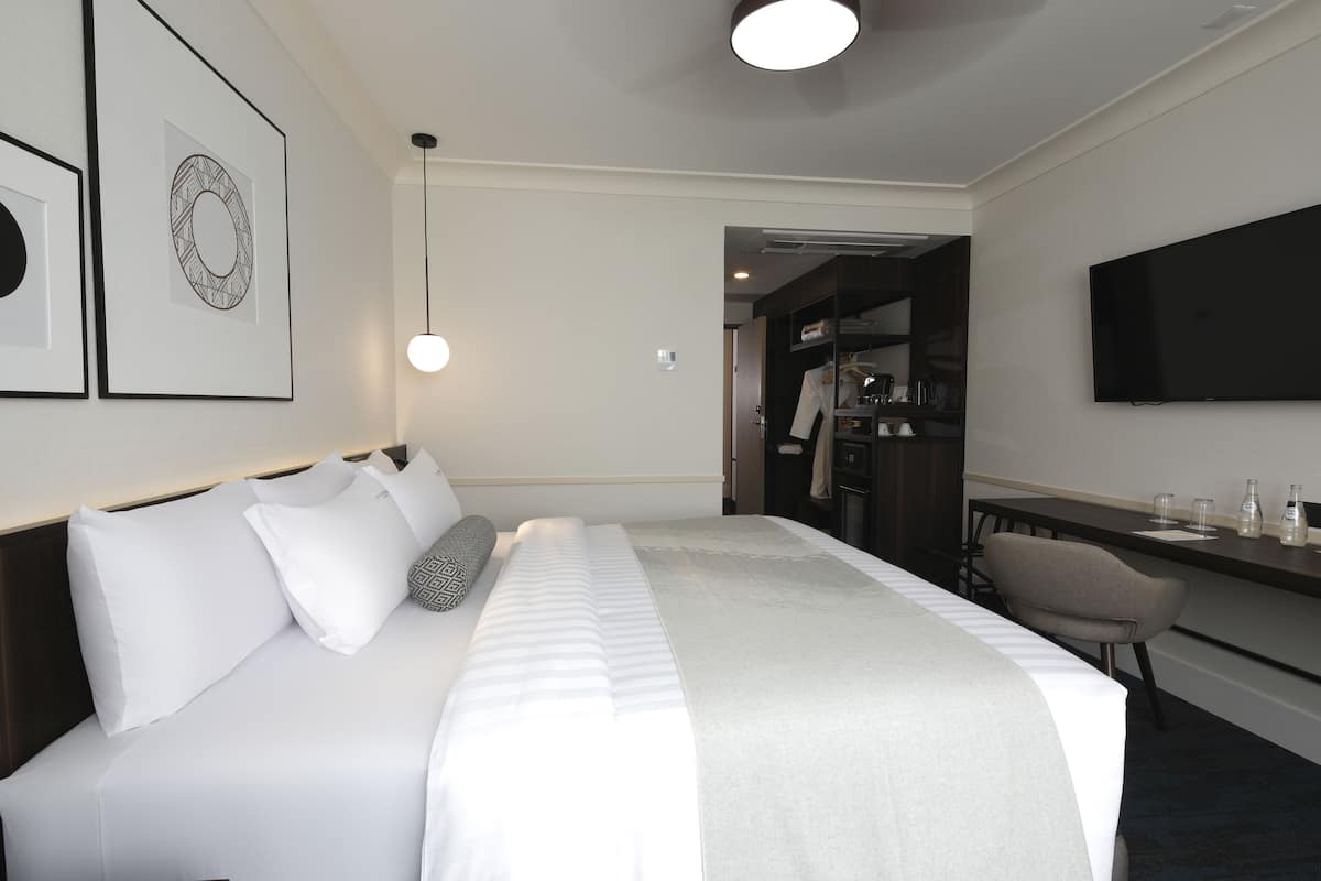 Quarto de hotel com uma cama grande, uma escrivaninha, uma televisão e um guarda-roupa.