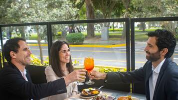 Uma mesa de jantar com pratos de comida, um copo de suco de laranja e uma pessoa segurando um copo.
