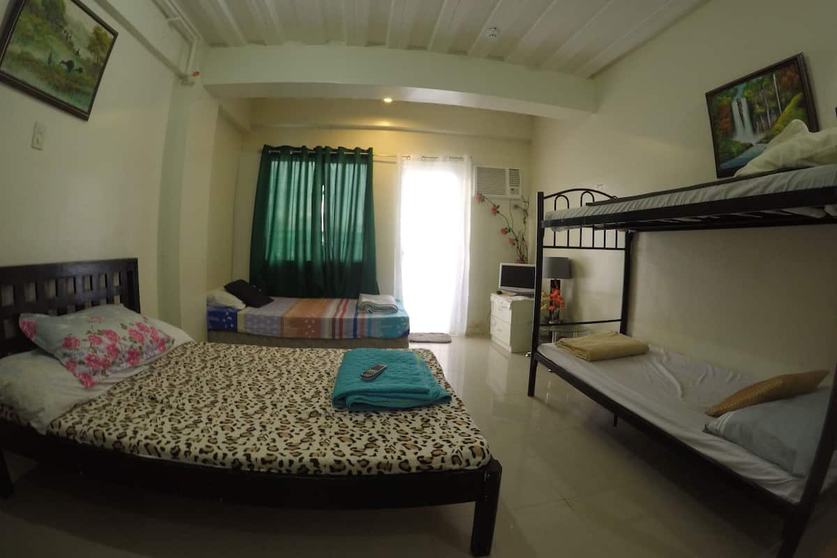 Quarto com cama, beliche, escrivaninha com computador e janela com cortinas.
