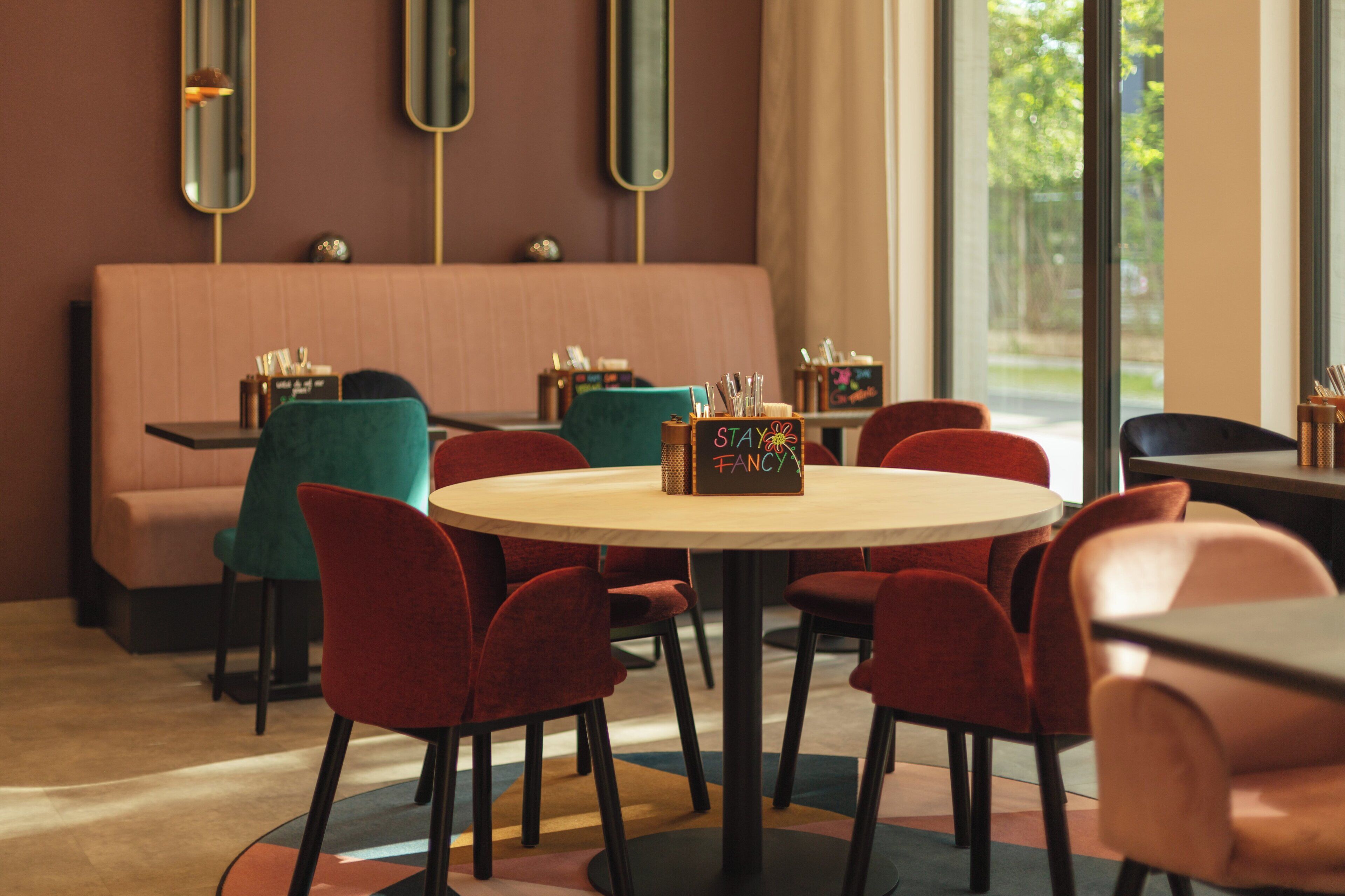 Um restaurante com mesas redondas, cadeiras vermelhas e uma área com assentos em cabine.