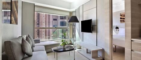 Sala de estar moderna com sofá, mesa de centro, TV e uma grande janela com vista para a cidade.