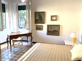 Quarto com cama, escrivaninha e cadeira. Três quadros emoldurados na parede.