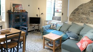 Uma sala de estar aconchegante com um armário azul, uma televisão, uma mesa de madeira e um sofá com almofadas estampadas.