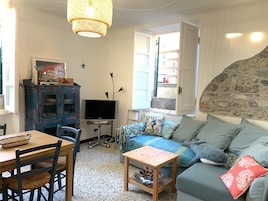 Uma sala de estar aconchegante com um armário azul, uma televisão, uma mesa de madeira e um sofá com almofadas estampadas.