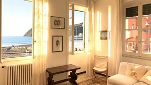 Quarto com vista para o mar, um sofá branco, uma mesa de madeira e uma cadeira.