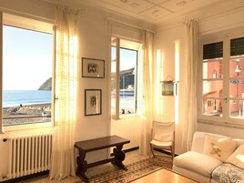 Quarto com vista para o mar, um sofá branco, uma mesa de madeira e uma cadeira.