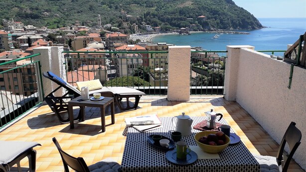 Uma varanda com mesa posta para o café da manhã, com vista para uma cidade costeira e o mar.
