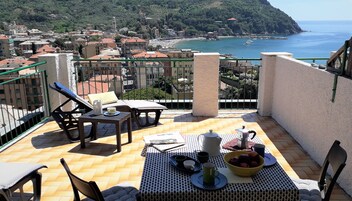 Uma varanda com mesa posta para o café da manhã, com vista para uma cidade costeira e o mar.