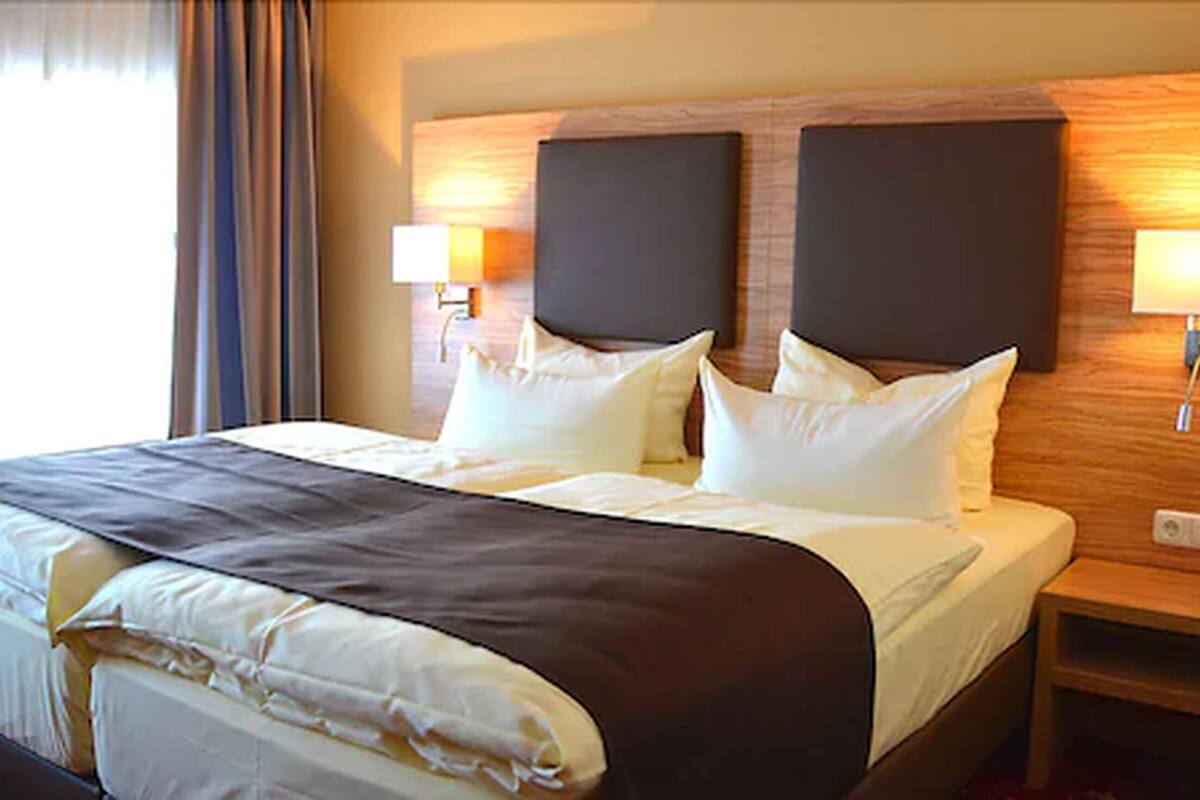 Quarto de hotel com uma cama grande, duas luminárias de cabeceira e uma cabeceira de madeira.