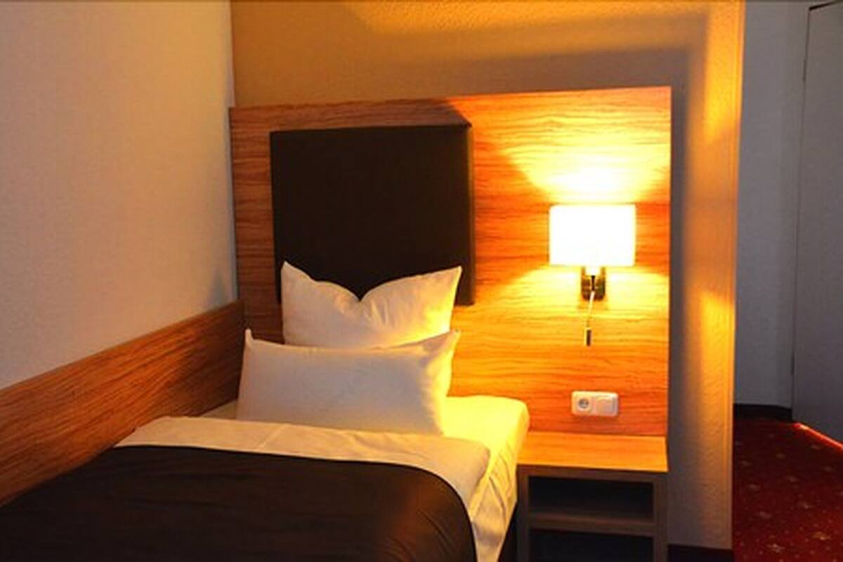 Quarto de hotel com cabeceira de madeira, abajur e uma mesinha.