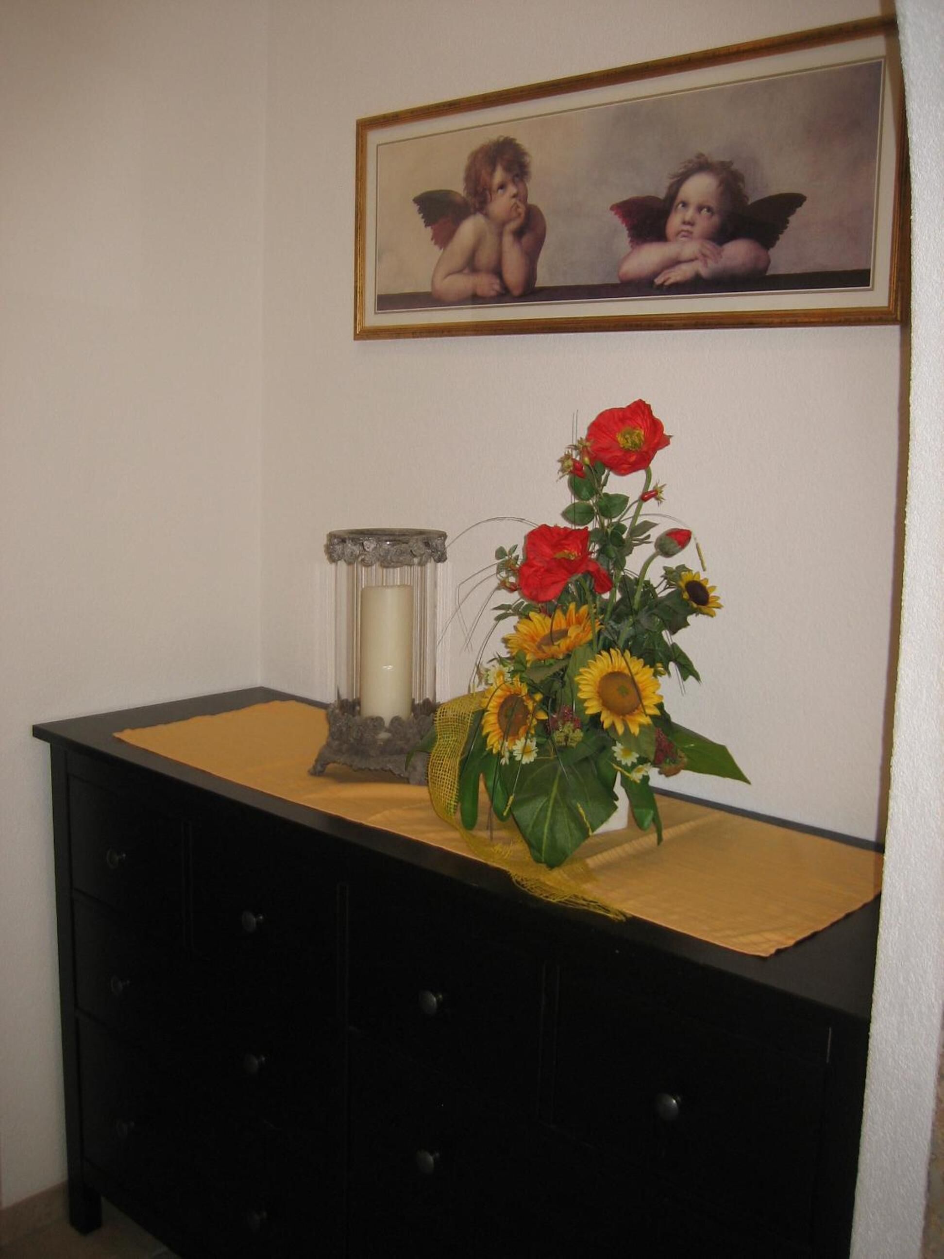Uma cômoda preta com um vaso de flores vermelhas e girassóis em cima.