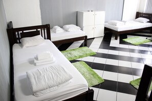 Quarto de hotel com duas camas, um guarda-roupa branco e chão quadriculado.