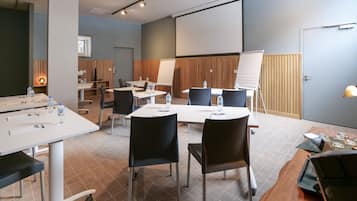 Uma sala de conferências com uma mesa grande, cadeiras, tela de projetor e quadro branco.