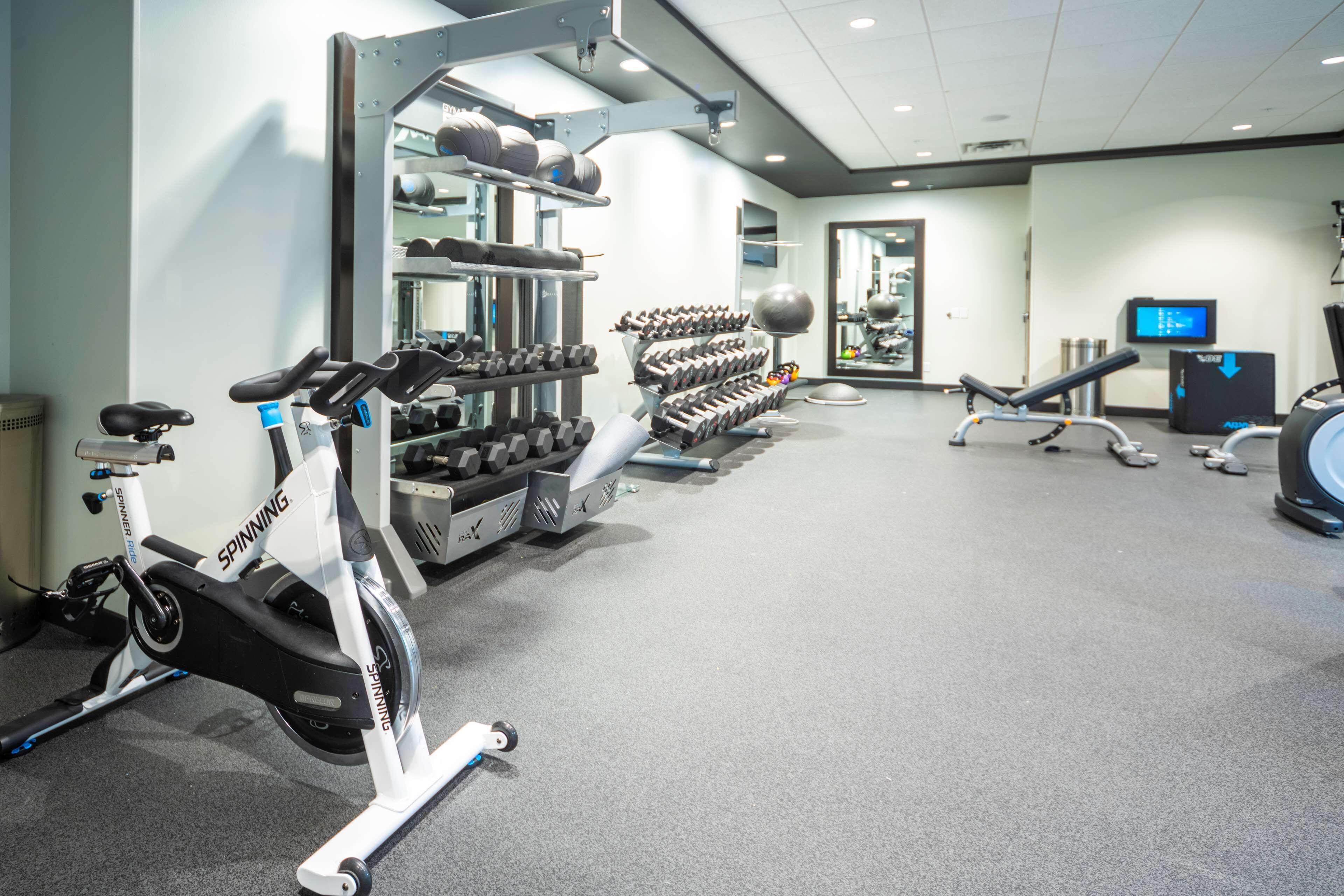 Uma academia com equipamentos de cardio, halteres e uma tela de televisão.
