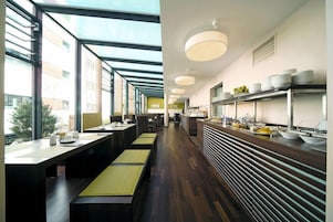 Um restaurante moderno com mesas comunitárias longas, um balcão com pratos e grandes janelas.