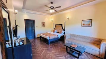 Quarto com cama, sofá, mesa de centro, ventilador de teto e uma porta.
