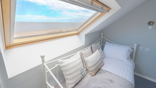 Quarto com claraboia, cama com roupa de cama listrada e vista para o mar.