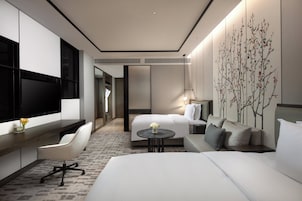 Quarto de hotel moderno com uma cama grande, uma escrivaninha com cadeira, uma mesinha redonda e uma televisão.