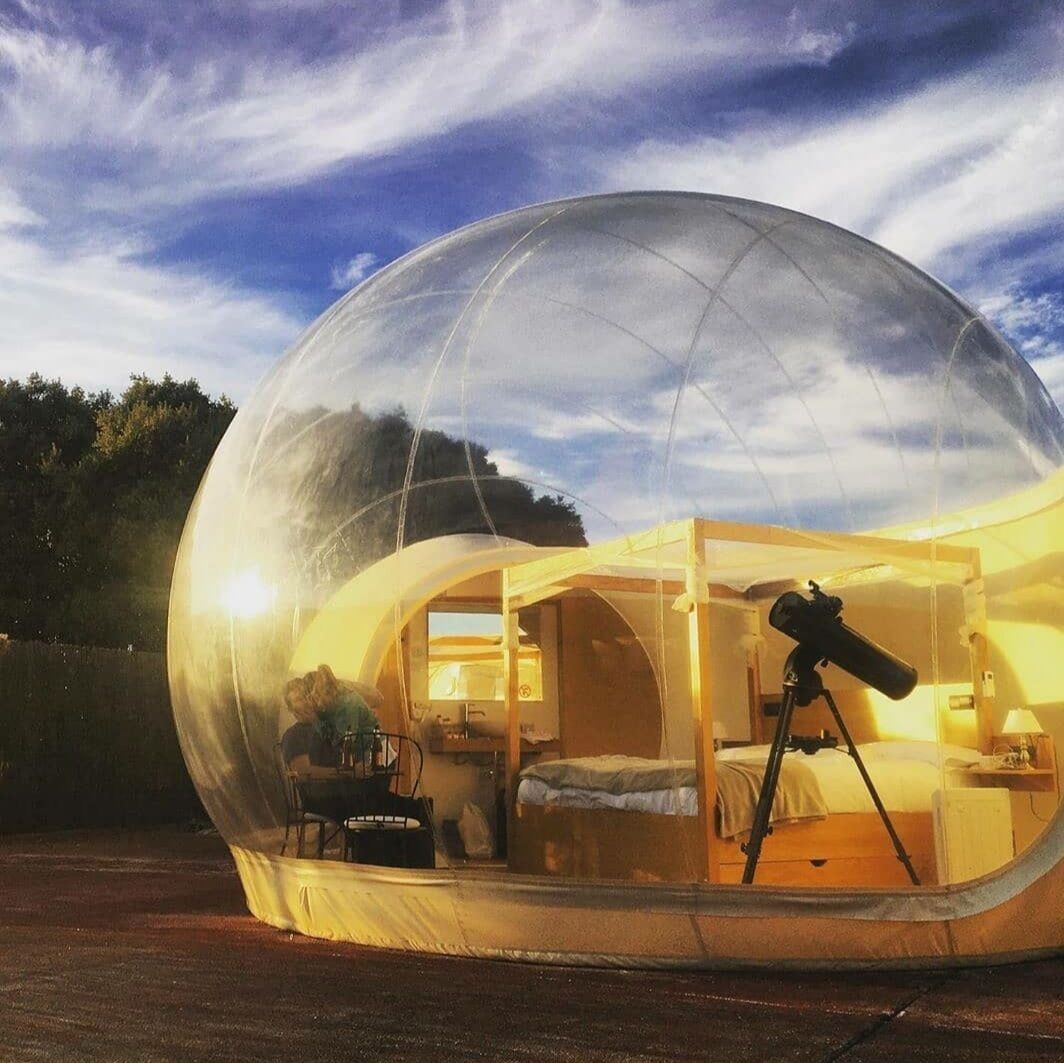 Estrutura em cúpula transparente com uma cama, uma cadeira e uma câmara sobre um tripé no interior.