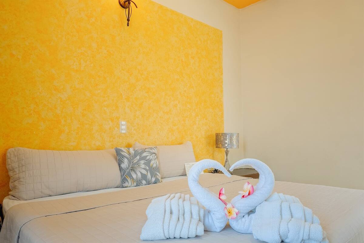 Quarto de hotel com cama, almofadas, abajur e duas toalhas dispostas em forma de coração.