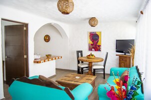 Uma sala de estar com sofá, mesa de centro, televisão e um espaço de jantar com cadeiras e mesa.
