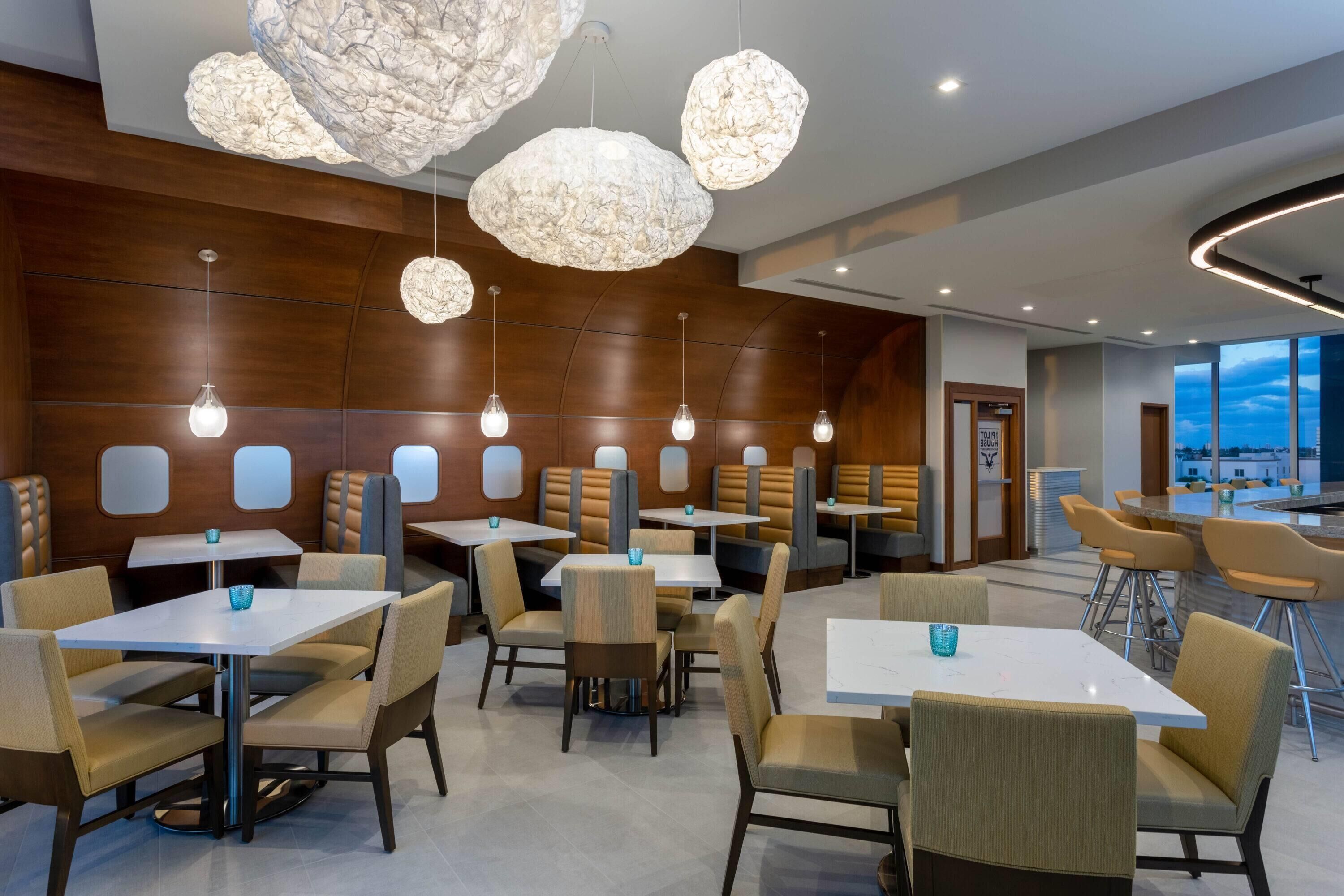 Uma sala de jantar moderna com mesas redondas, assentos acolchoados e luminárias pendentes com texturas diferenciadas.
