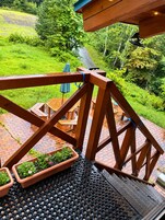 Um deck de madeira com guarda-corpo de metal, vasos com plantas e um pátio de tijolos.