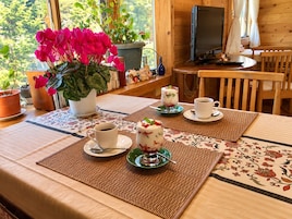 Quarto aconchegante com uma mesa de jantar posta para dois, televisão e janela com vista para o verde.