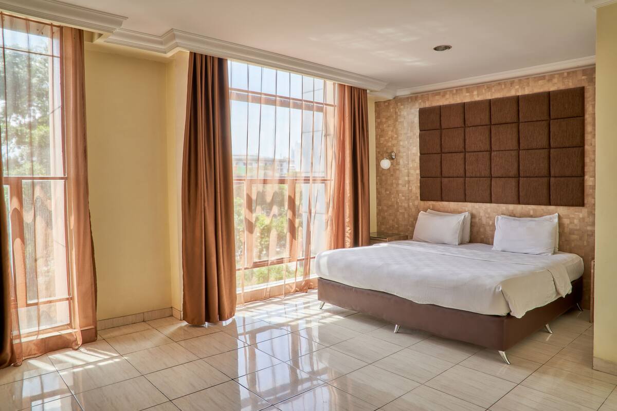 Quarto com cama grande, vista pela janela e piso cerâmico.